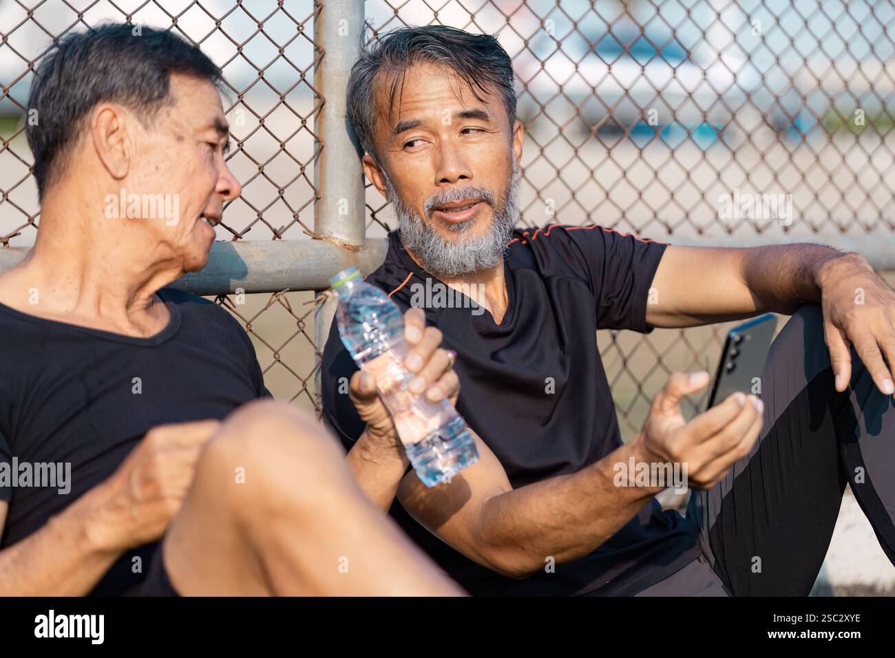 Engaged senior Asian men discussing wellness while resting on a sports ...