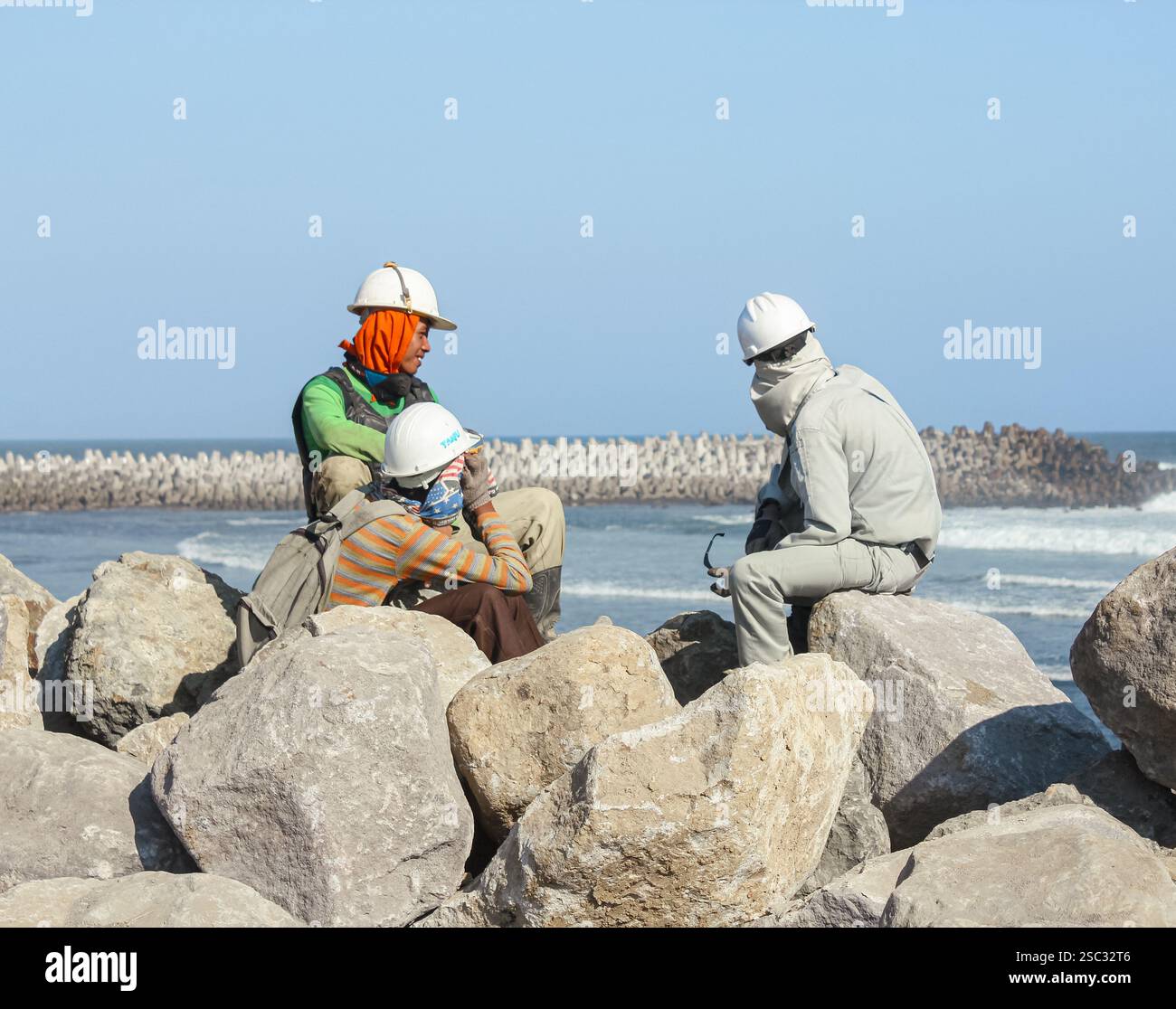 Three construction workers in white hard hats are sitting on large ...