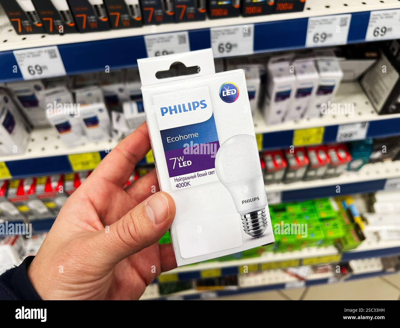 Kyiv, Ukraine - February 04, 2025: Hand holding Philips 7W LED light bulb box in a store aisle ...