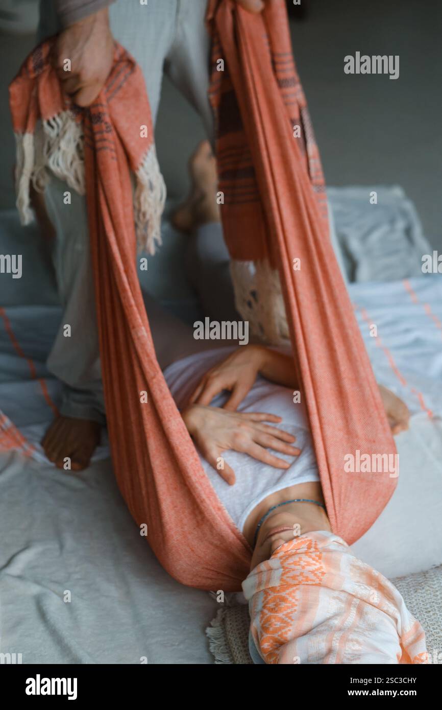 A practitioner supports a person lying on the floor, using soft fabric ...