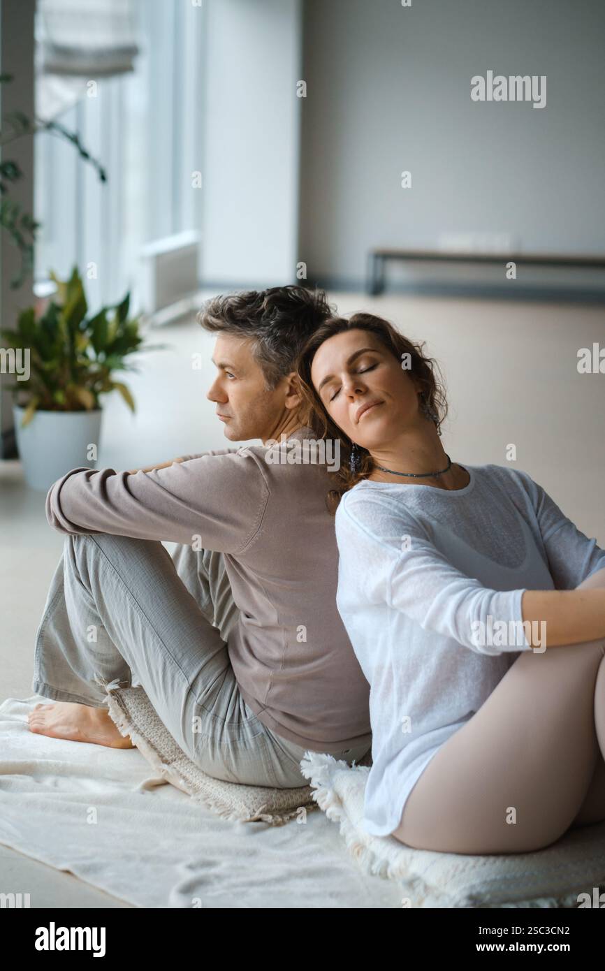 A man and woman sit back to back on a soft mat, surrounded by a ...