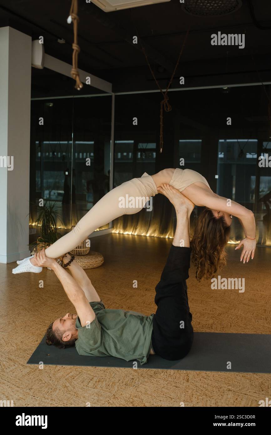 In a bright studio, a couple engages in acro yoga, showcasing a balance ...