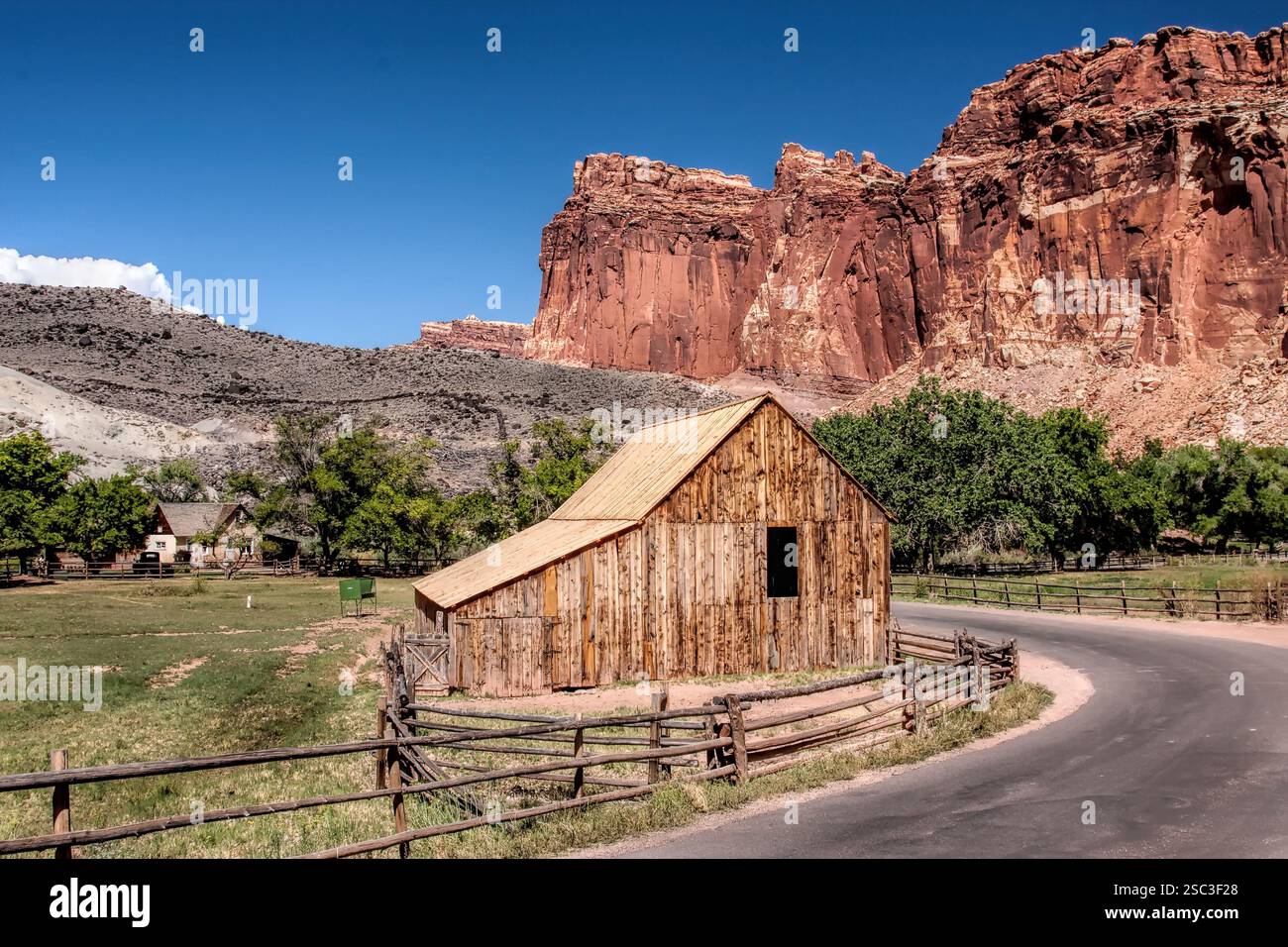A small wooden building with a slanted roof sits on a dirt road. The ...