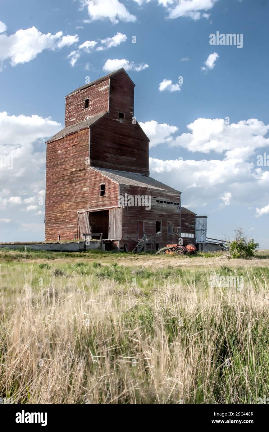 A red grain silo is in a field. The silo is empty. The silo is old and ...