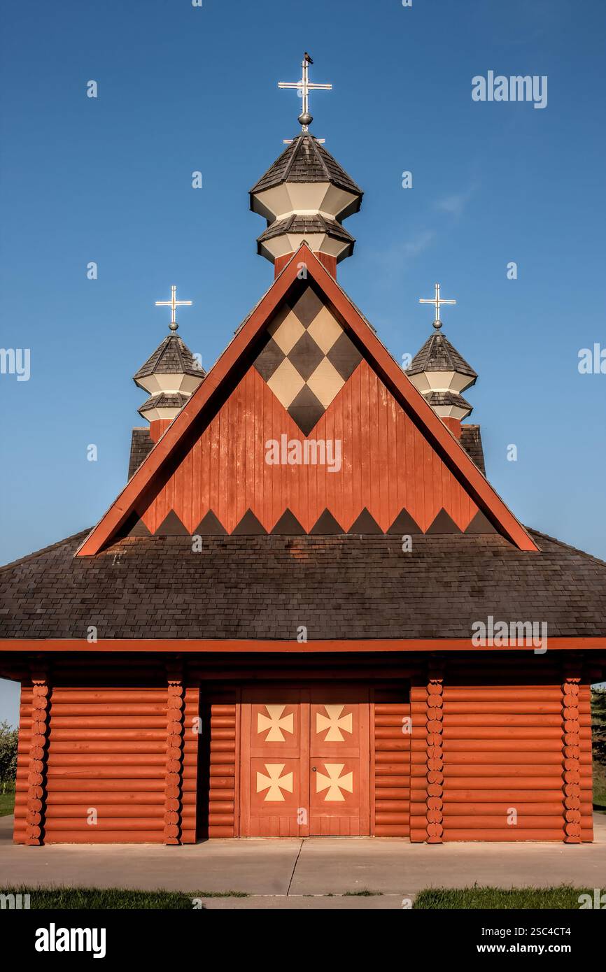 A small red building with a cross on the roof. The roof is made of wood ...