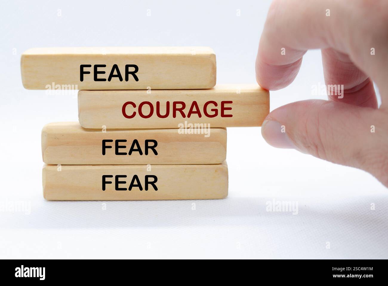 Hand pulling out wooden block with text saying COURAGE to separate from ...