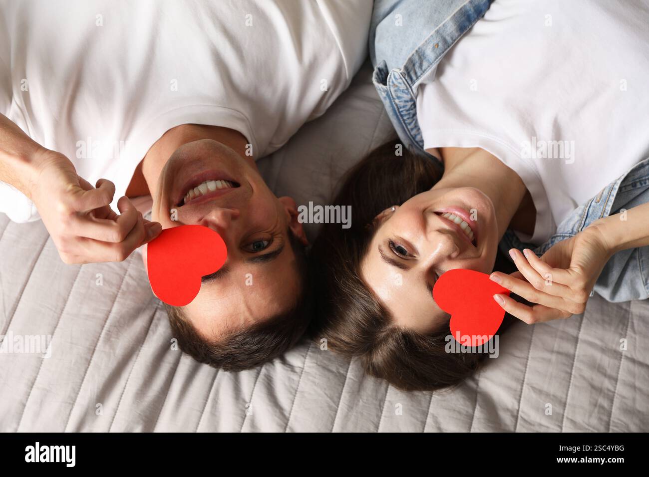 Lovely couple with paper hearts on bed, top view. Valentine's day ...