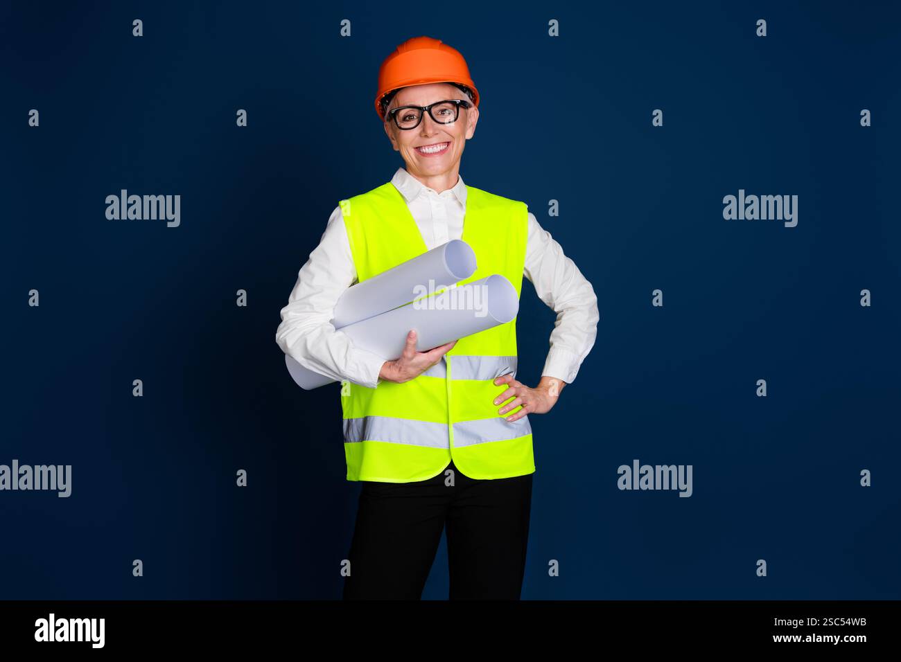 Confident female architect in high visibility vest and helmet holding ...