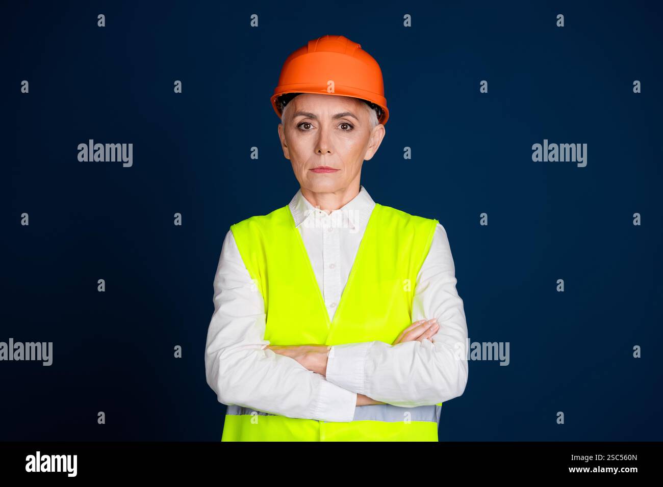 Confident mature woman in safety gear standing against dark blue ...