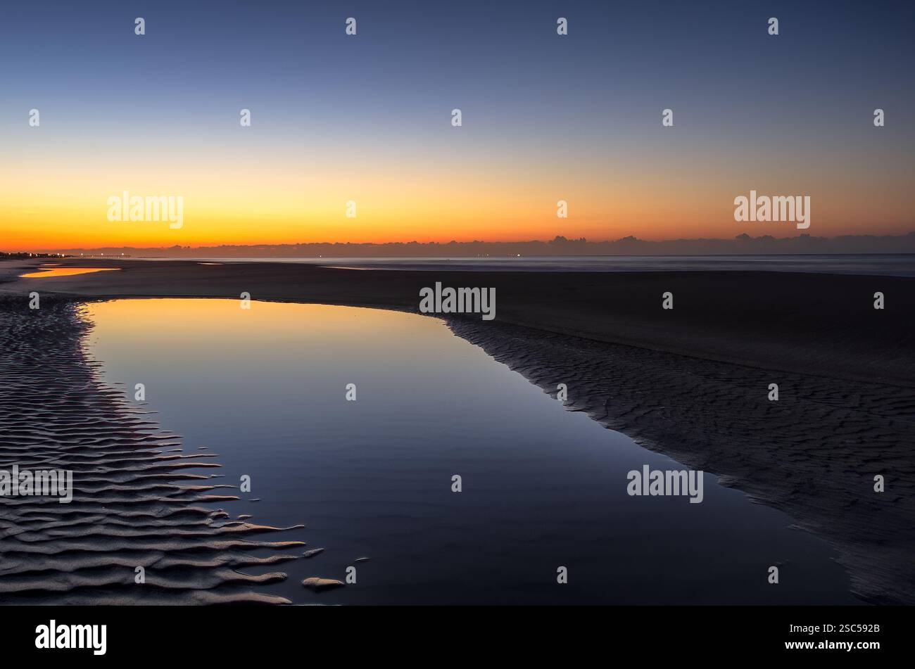 Scenic twilight over a tidal pool on a beach, reflecting golden hues of ...