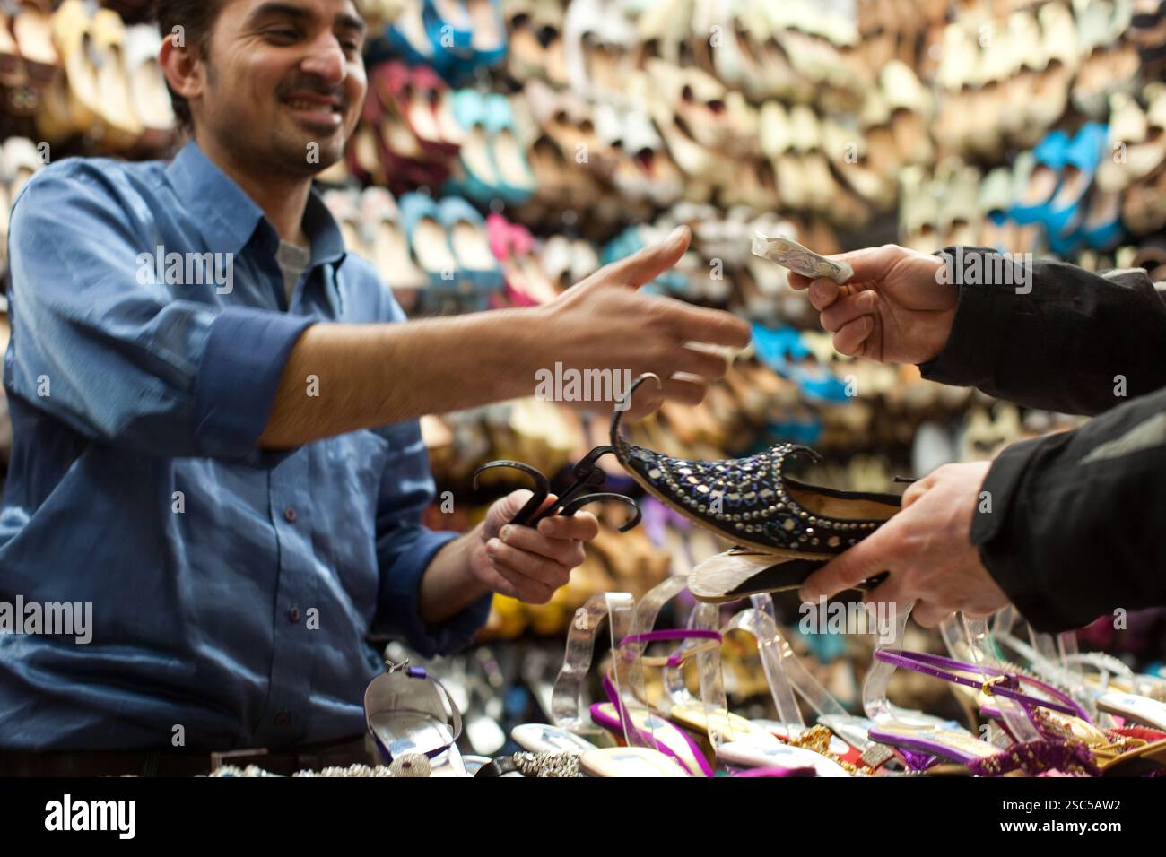 A man purchases traditional shoes at a bustling market stall filled ...