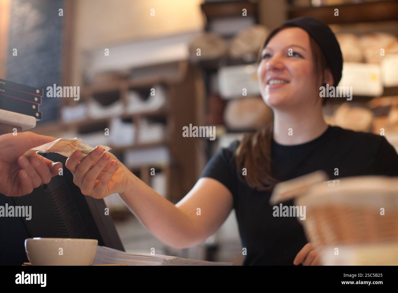 A cashier hands change to a customer in a bakery setting Stock Photo ...
