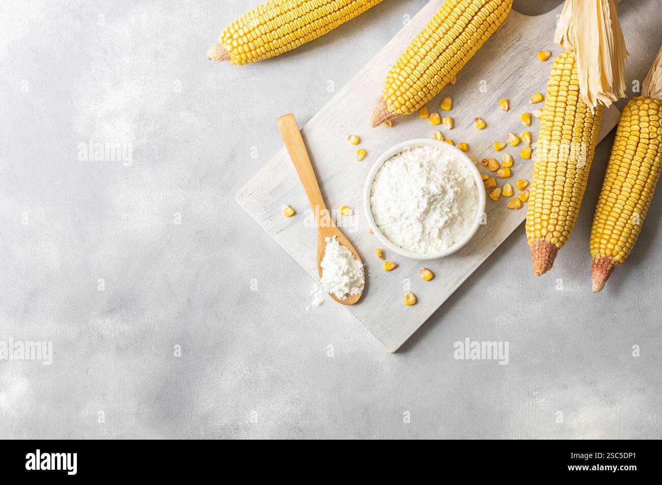 Corn starch in bowl and spoon with dried corn groats, kernels on rustic ...