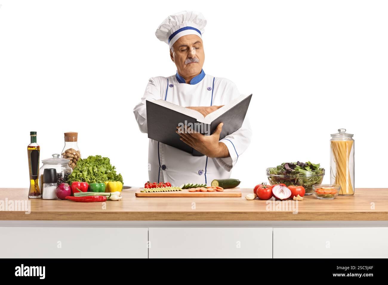 Mature male chef reading a cook book and cooking pasta and vegetables ...