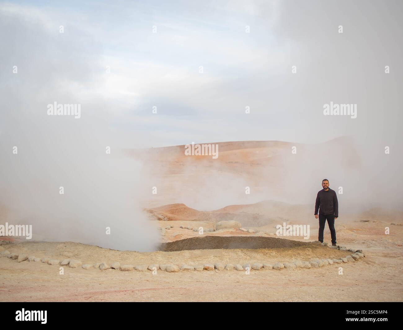 a traveler man posing by the gas vents of the Uyuni salt flat geyser in ...