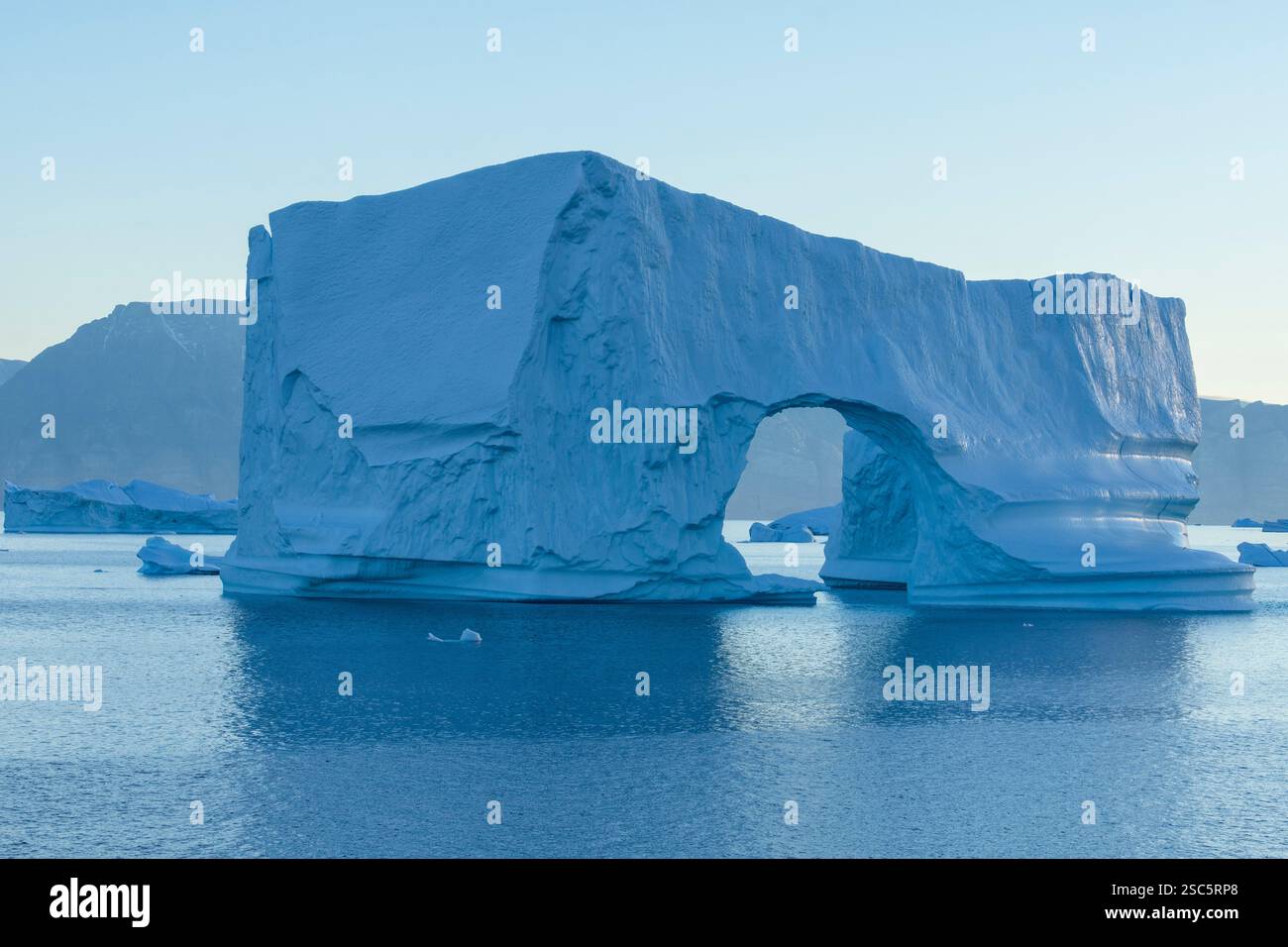 An iceberg with an arch floats together with many other icerbergs in ...