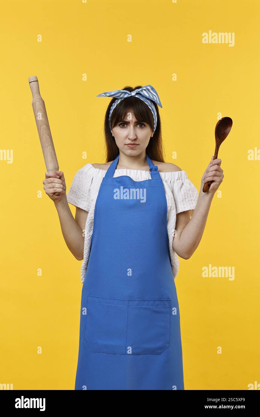Angry woman with rolling pin and spoon on yellow background Stock Photo ...