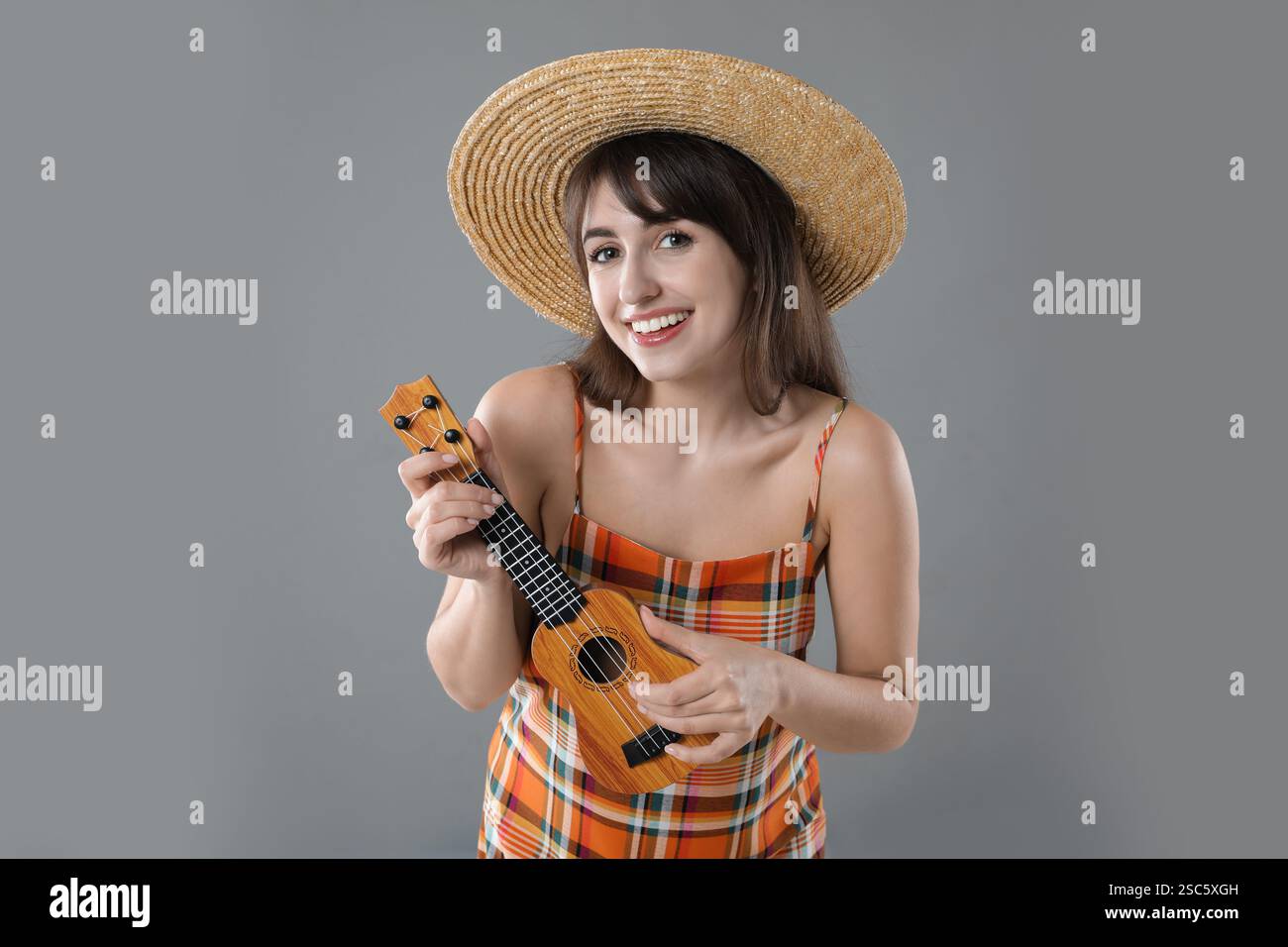 Happy woman playing ukulele on grey background Stock Photo - Alamy