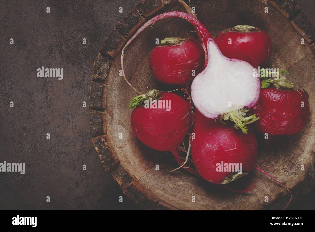 Fresh red radishes are displayed on a rustic wooden cutting board ...