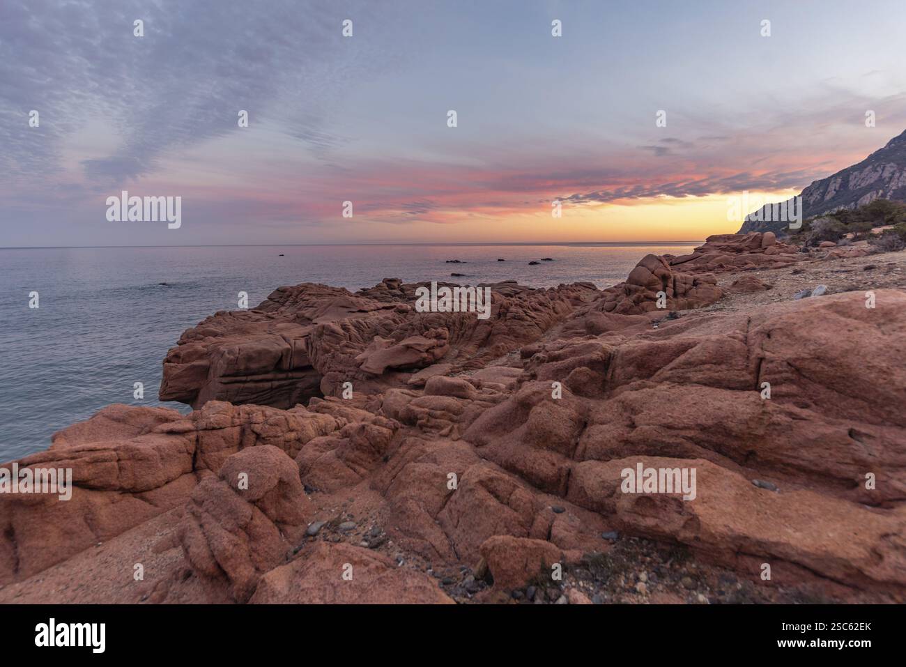 Large red rocks at the edge of the sea under a cloudy evening sky ...
