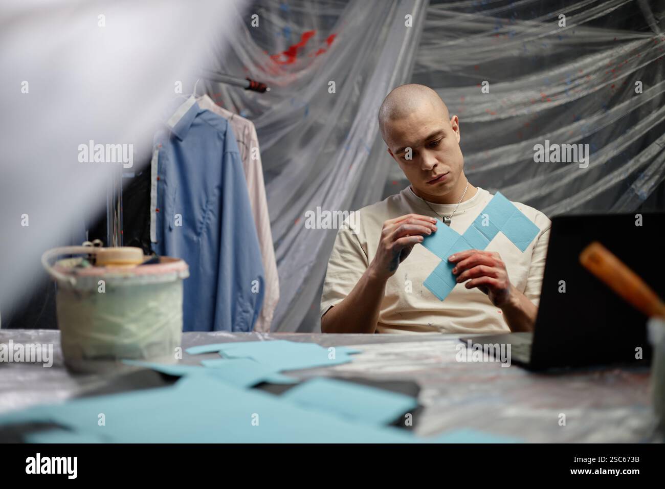 Medium shot of adult male artist with buzz cut sitting at table ...