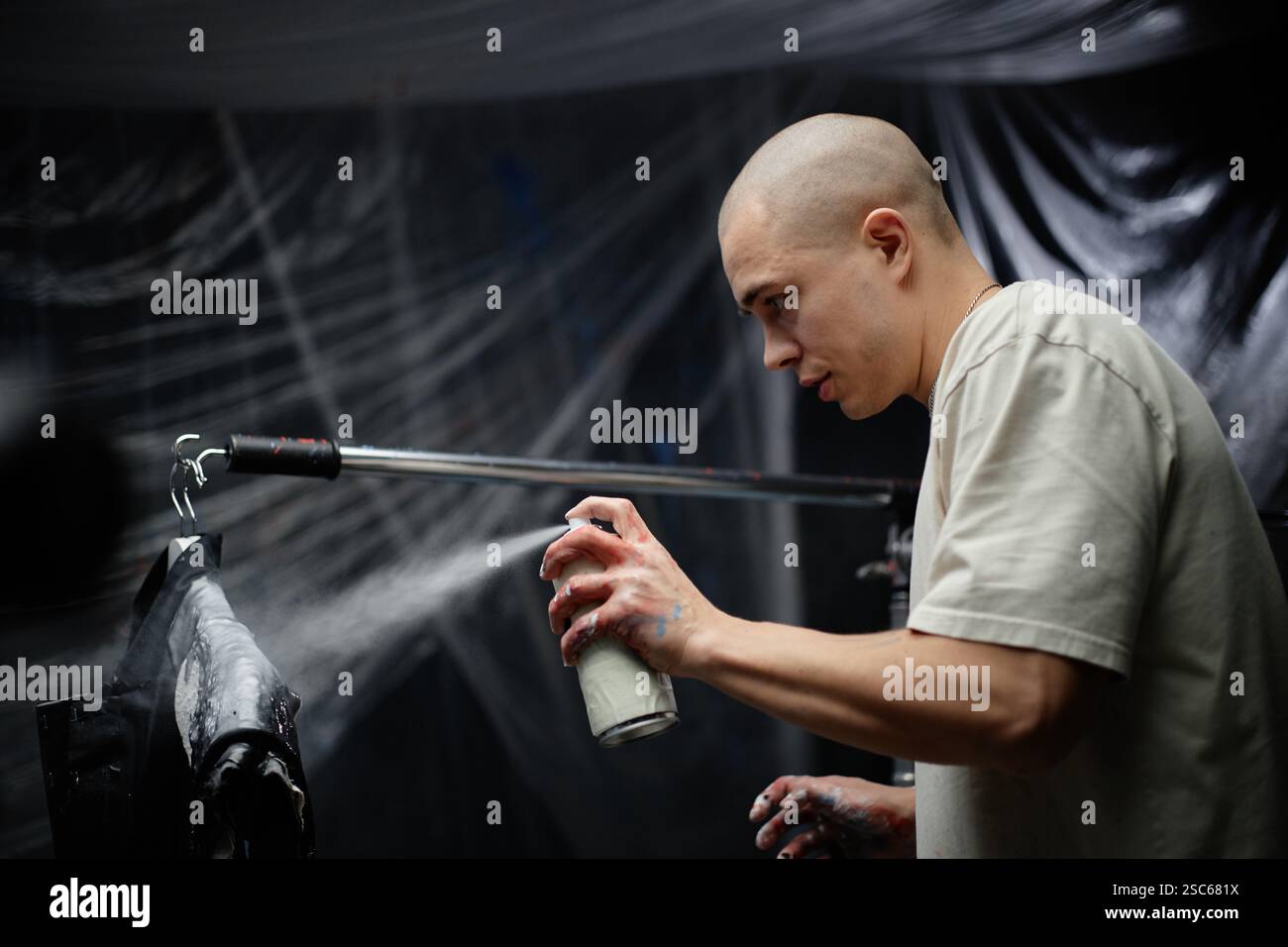 Side view of concentrated male artist with buzz cut spraying white ...