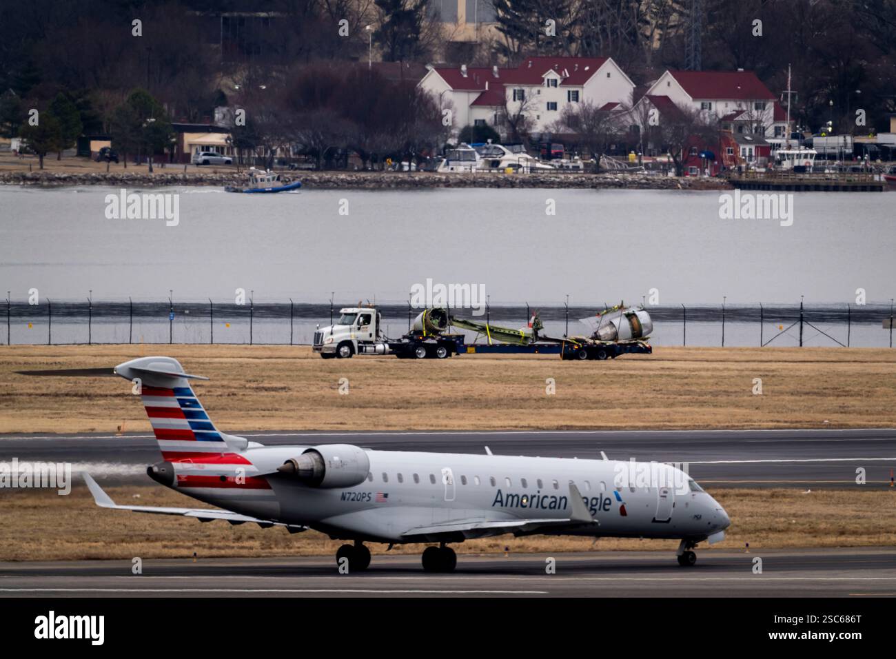 An aircraft lands on the runway as a flatbed truck carries away ...