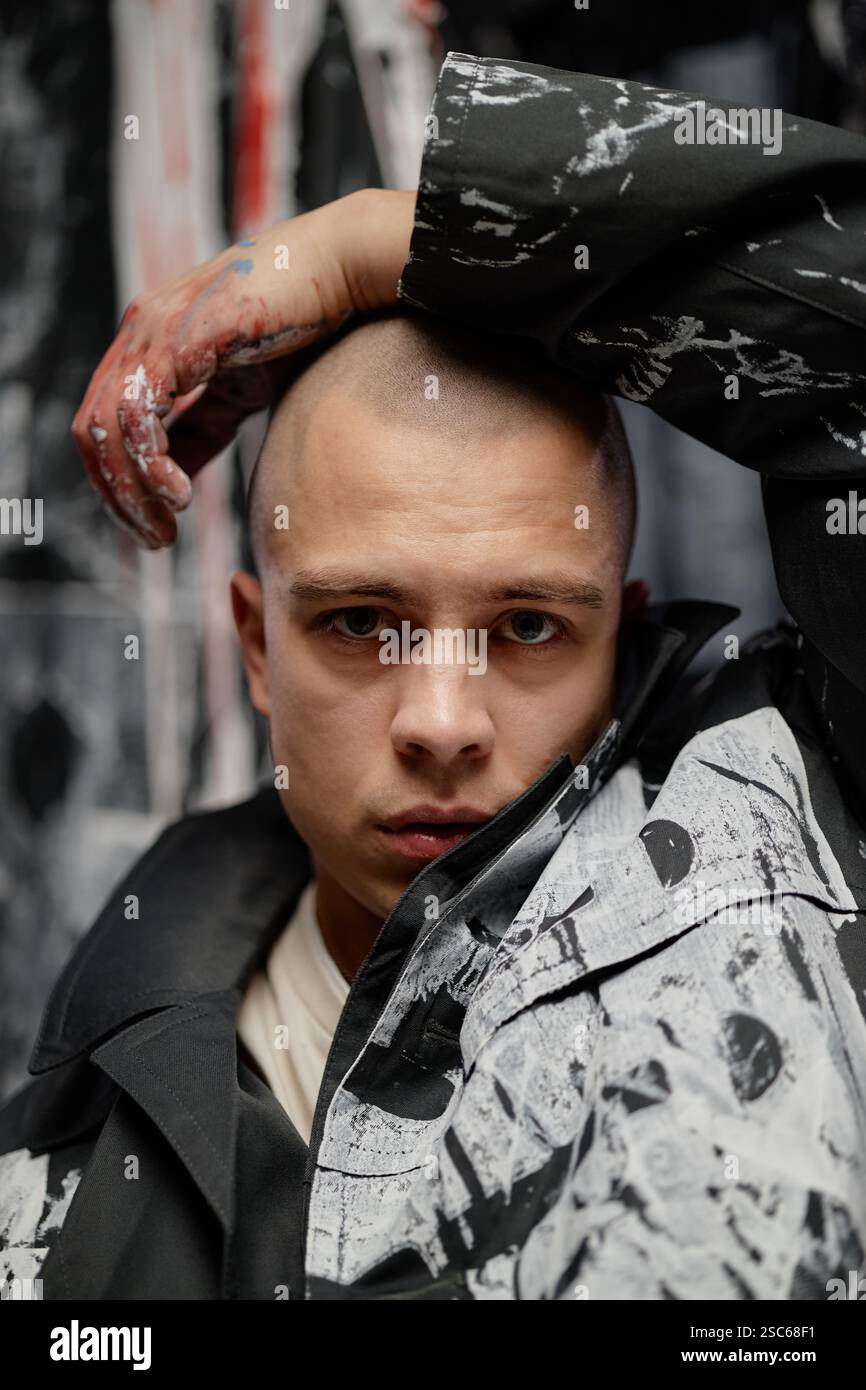 Vertical portrait of male fashion artist with buzz cut posing with arm ...