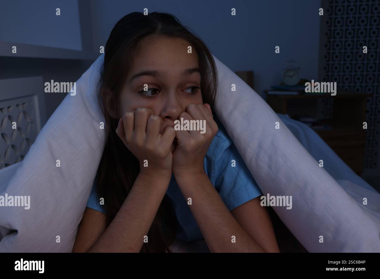 Afraid girl hiding under duvet on bed at night Stock Photo - Alamy