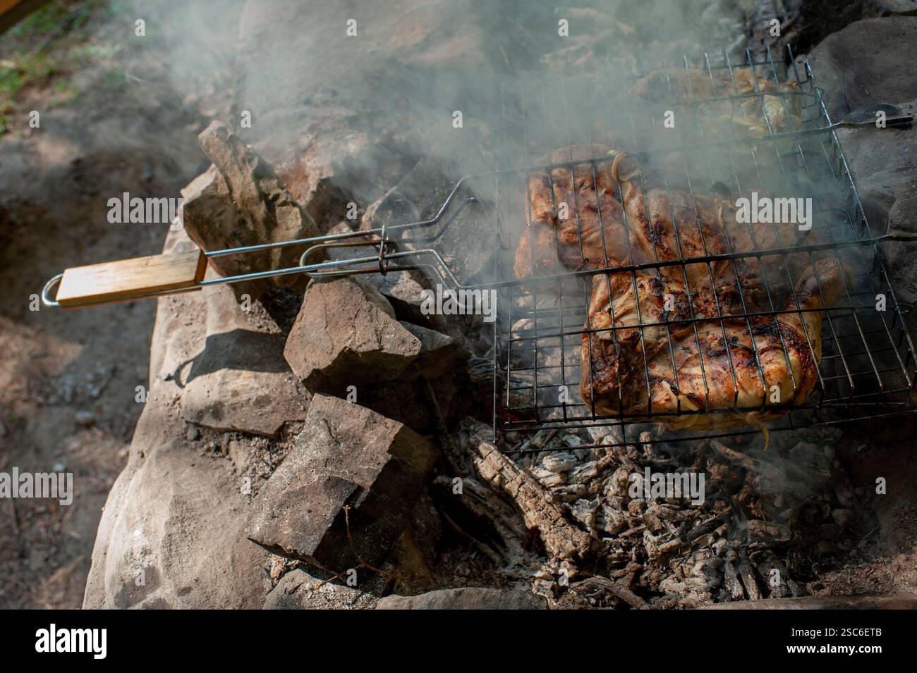 Marinated chicken on a barbecue in the forest. Meat is roasted on coals ...