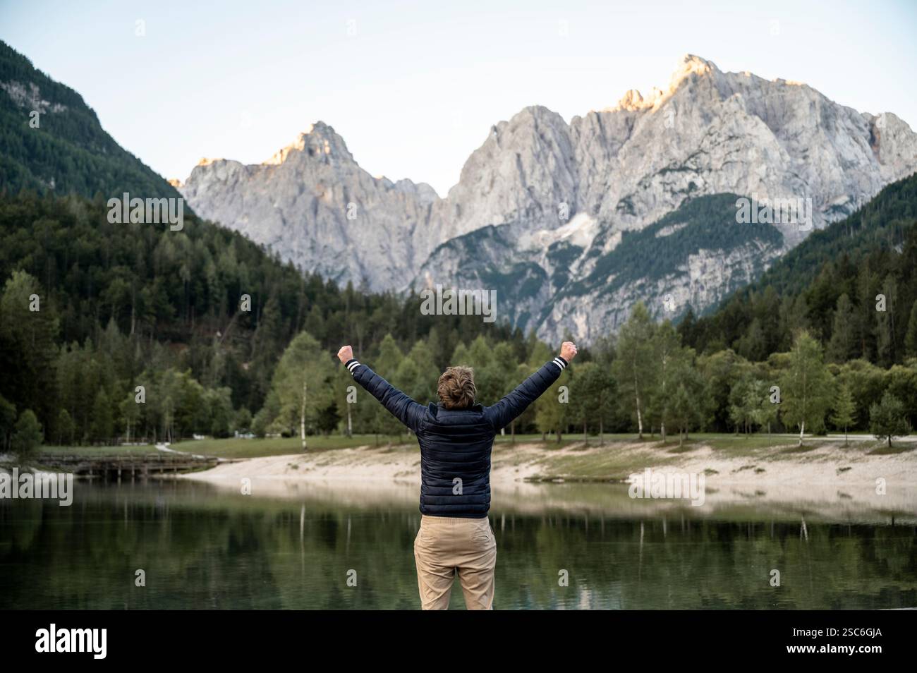 A person stands triumphant before a serene alpine lake, arms raised in ...