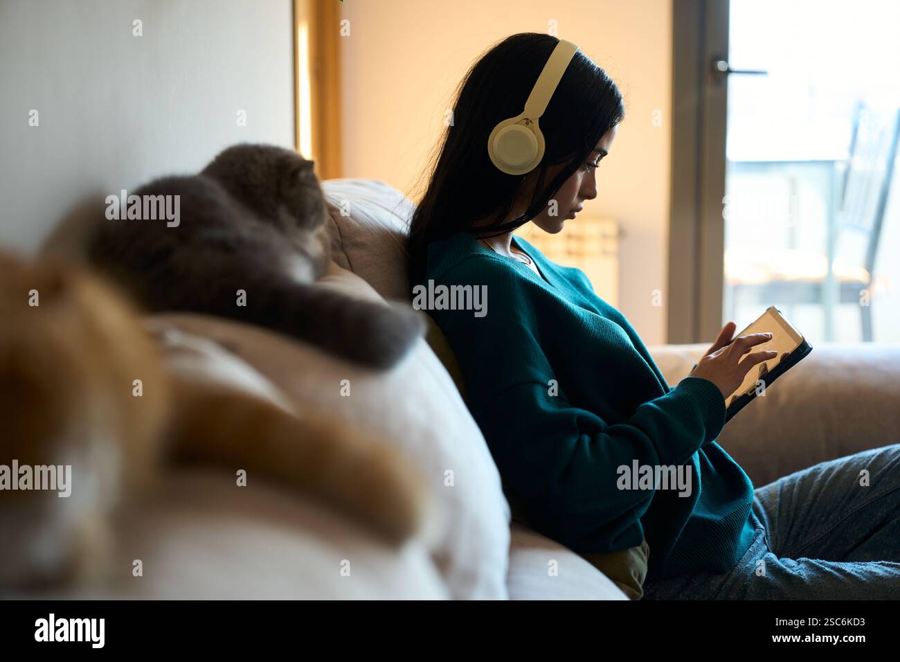 Cozy home scene of a young woman enjoying music and browsing on her ...