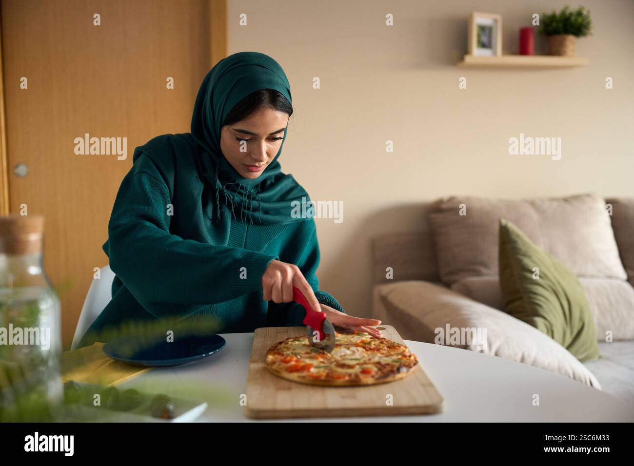 Muslim woman cutting pizza at home with pizza cutter Stock Photo - Alamy
