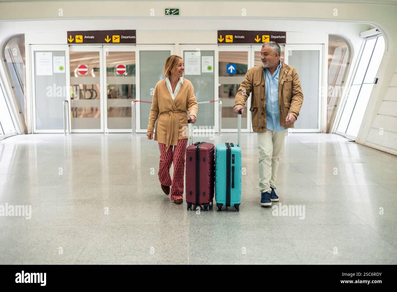 Cheerful senior couple pulling suitcases walking through airport ...
