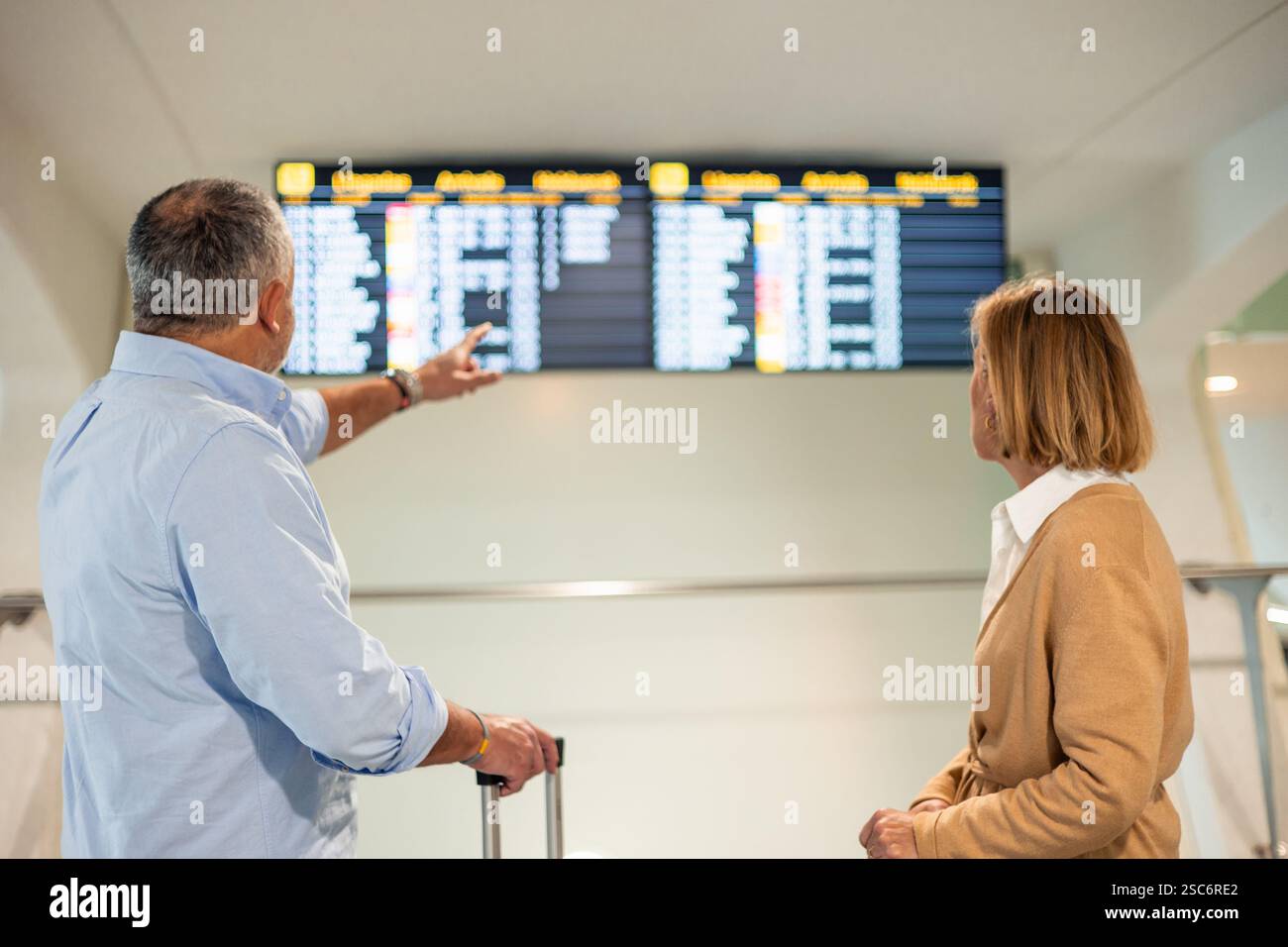 Senior couple looking at the airport timetable display, checking their ...