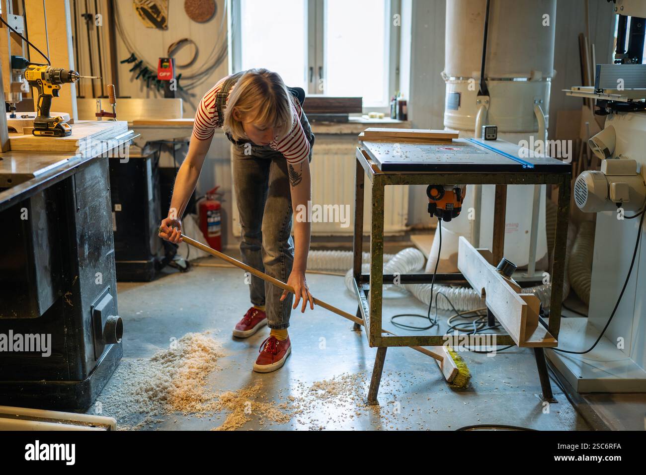 Carpenter woman cleanup workshop after woodwork. Handywoman sweep ...