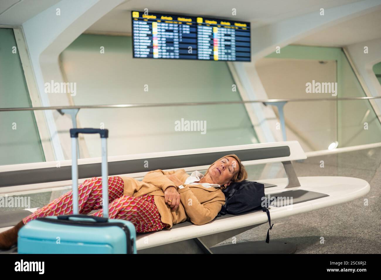 Senior woman sleeping on a bench at the airport terminal while waiting for her flight departure ...