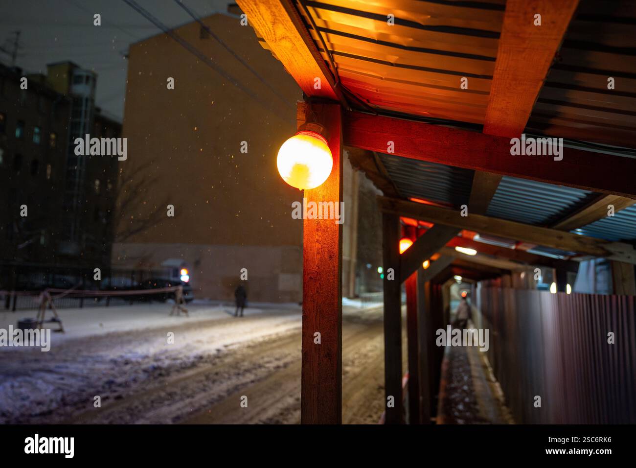 Snowstorm through construction site, canopy with lamps casting warm ...