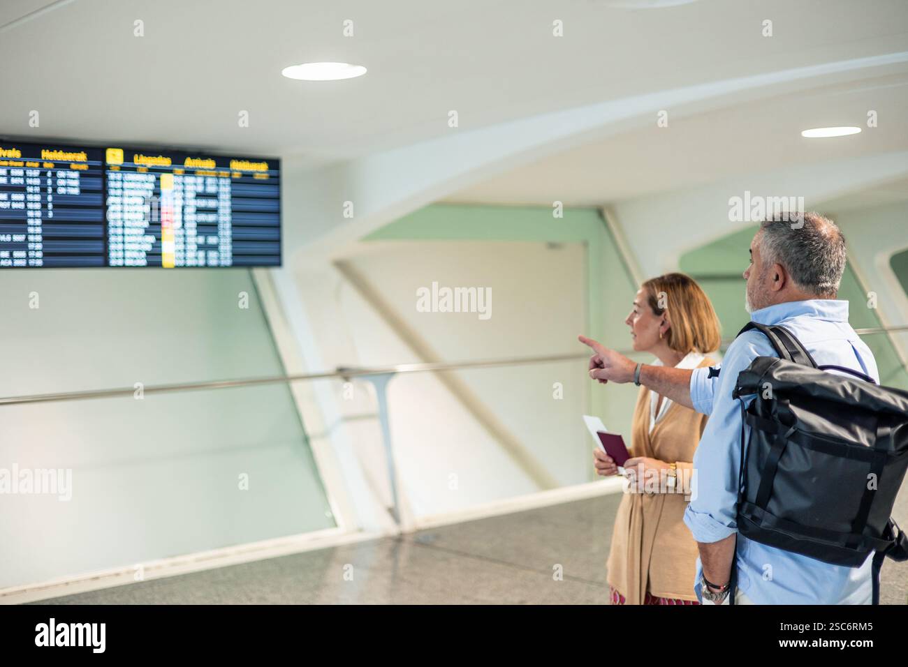 Senior couple holding passports and boarding passes checking flight information on airport ...