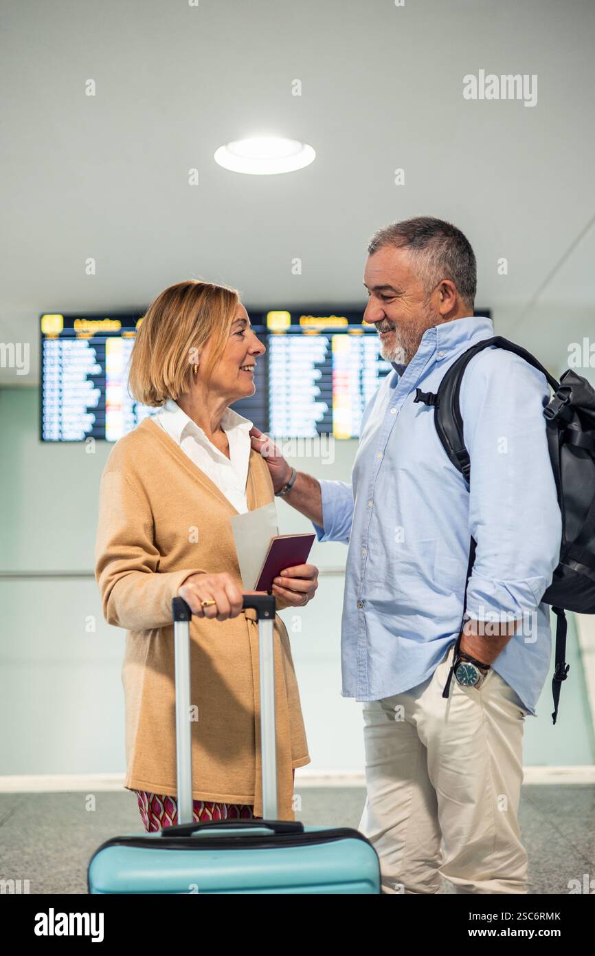 vertical Senior couple holding passport and boarding pass smiling at each other at the airport ...