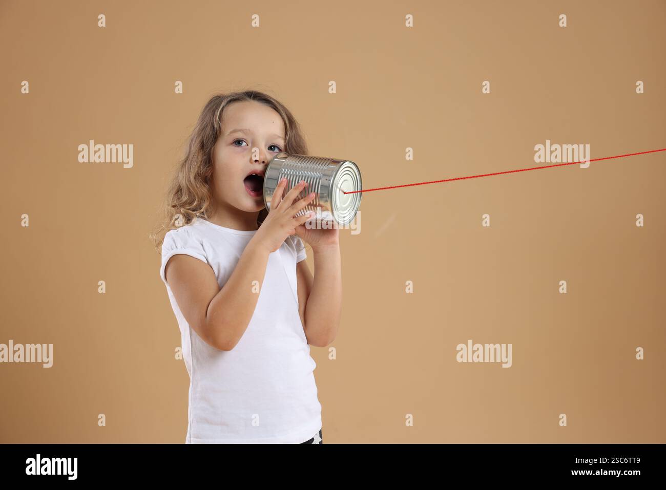 Girl using tin can telephone on beige background Stock Photo - Alamy
