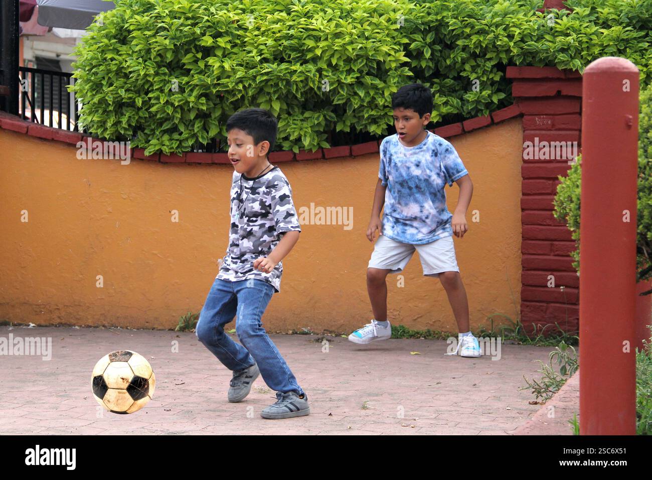 Two 9-year-old poor dark-skinned Latino boys play soccer in the street ...