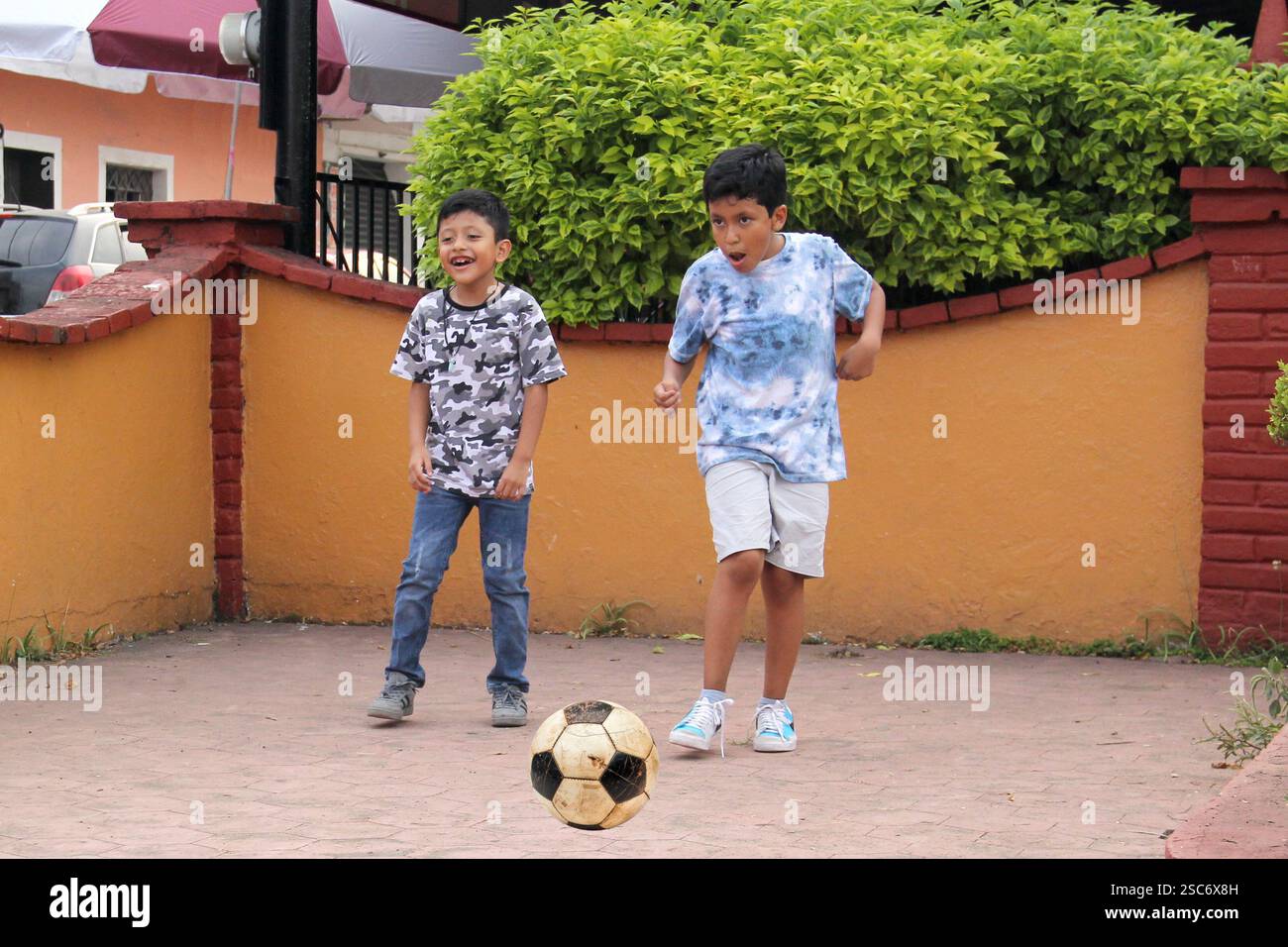 Two 9-year-old poor dark-skinned Latino boys play soccer in the street ...