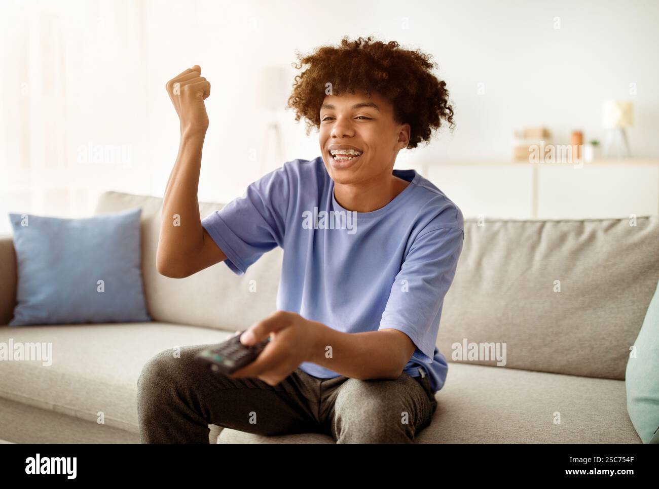 Excited African American teen with remote control enjoying movie ...