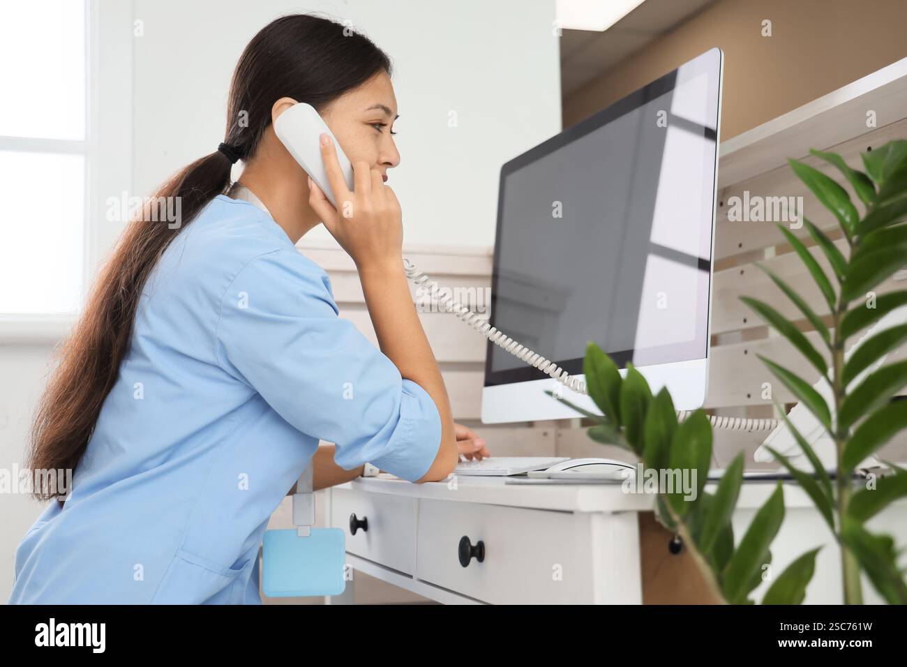 Female Asian medical intern talking by telephone at reception in clinic ...