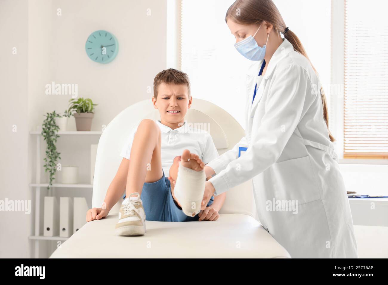 Female doctor examining little boy's injured leg on couch in clinic ...