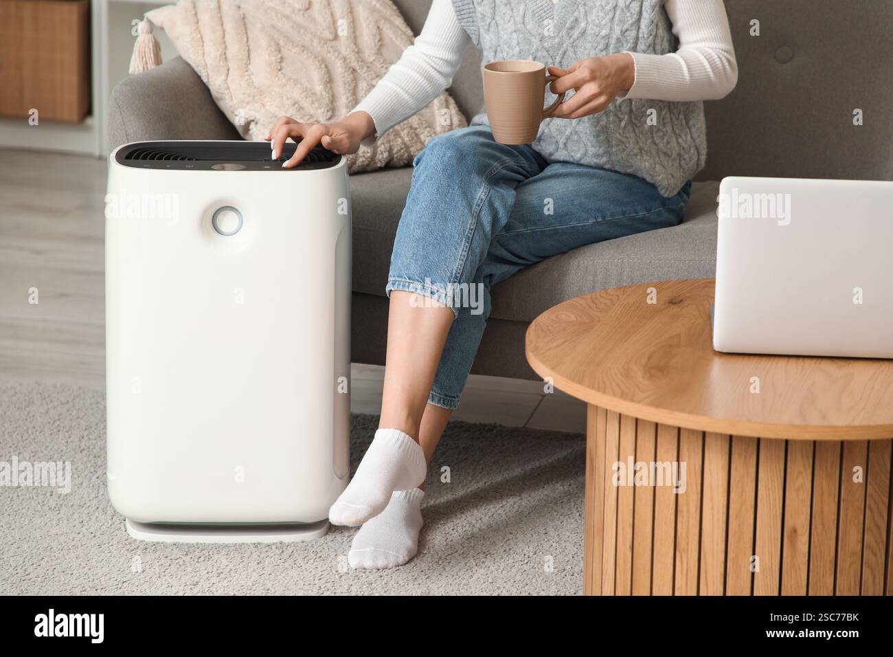 Young woman with cup of tea turning on air purifier at home Stock Photo ...