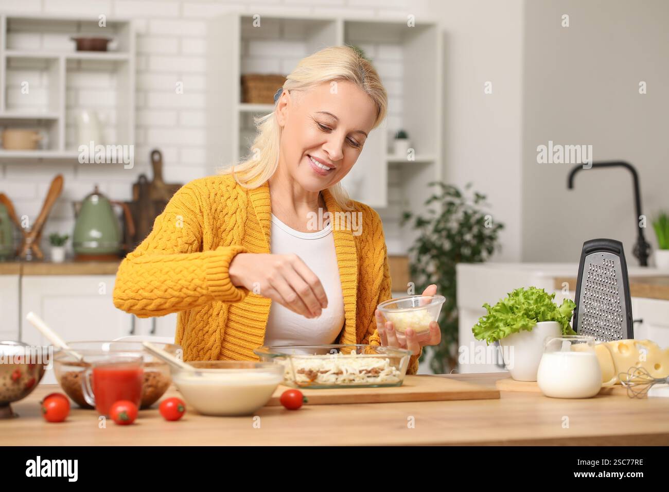 Beautiful mature happy woman adding cheese to delicious lasagna at ...