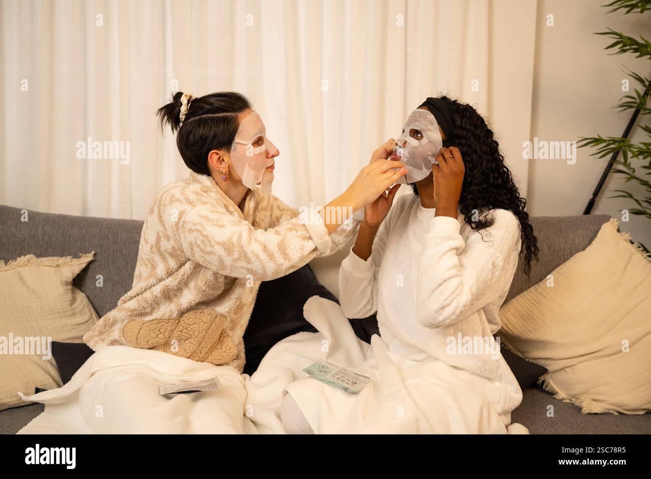 Two friends wearing bathrobes are sitting on a sofa in their living ...