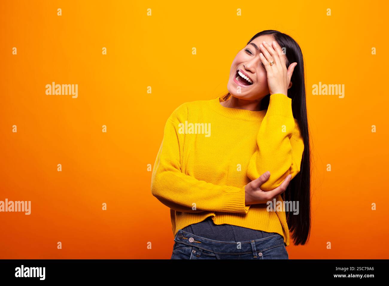 Asian woman smiles and playfully hides her face, expressing a shy yet ...